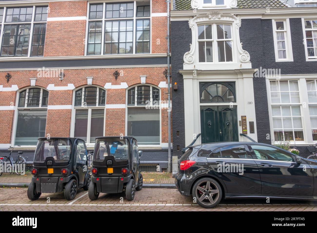 Netherlands. Small cobbled street in Amsterdam. Two mini cars are ...