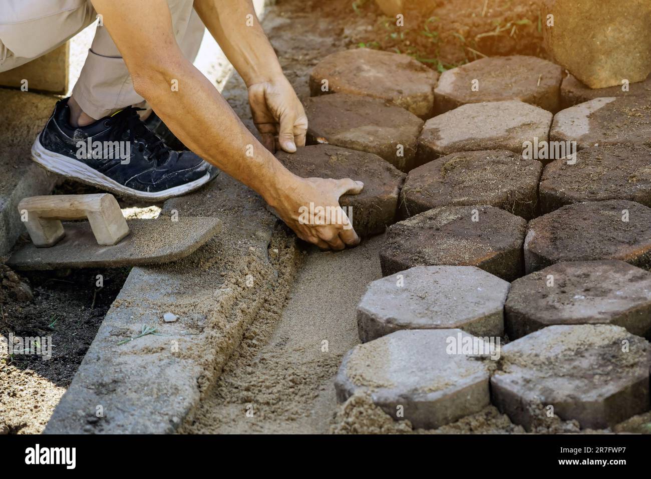 Hands of workman make it fit and to place stone pavers in a row ...
