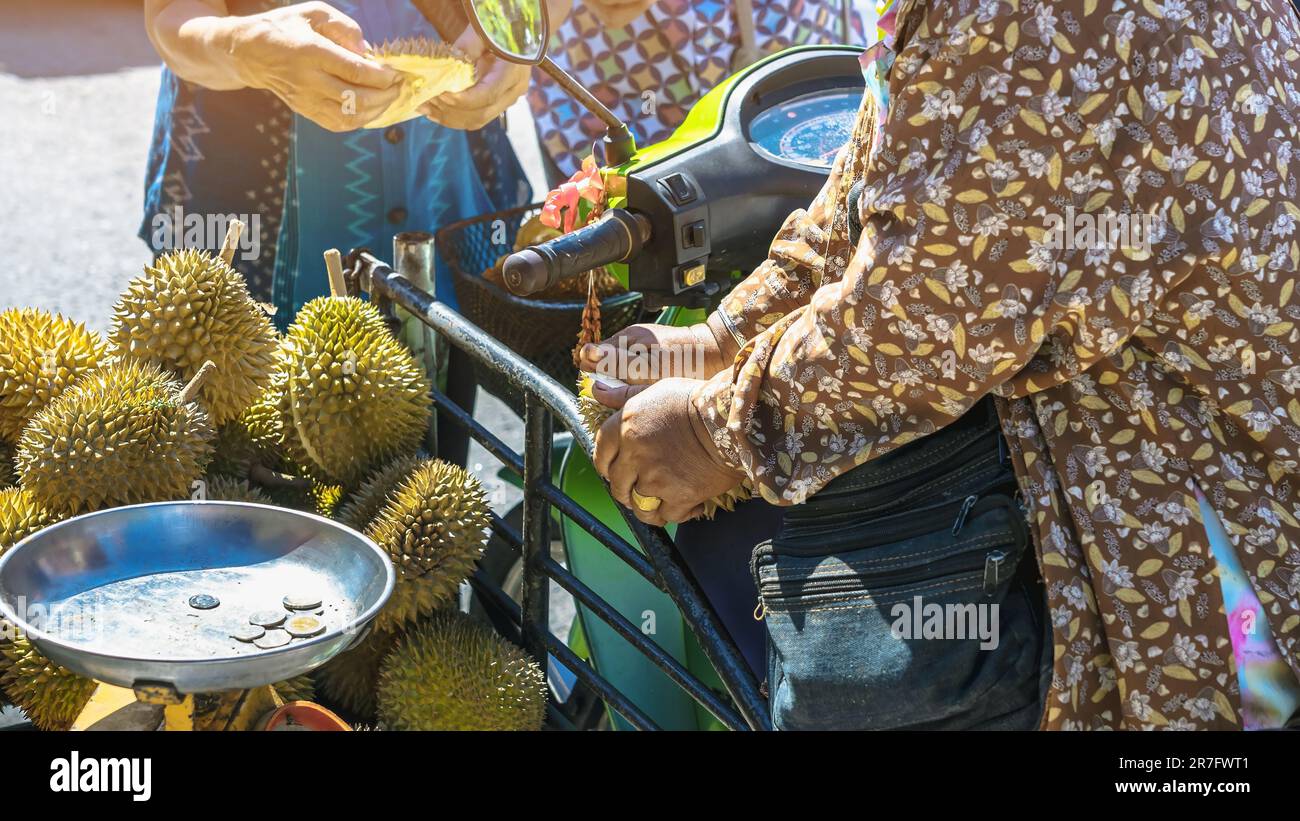 Elderly Thai female vendor ride motorcycle selling durians and fruits ...