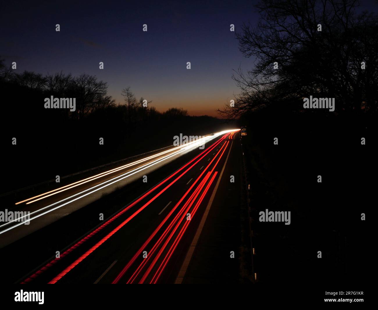 A time lapse of a busy highway at night, illuminated by the headlights ...