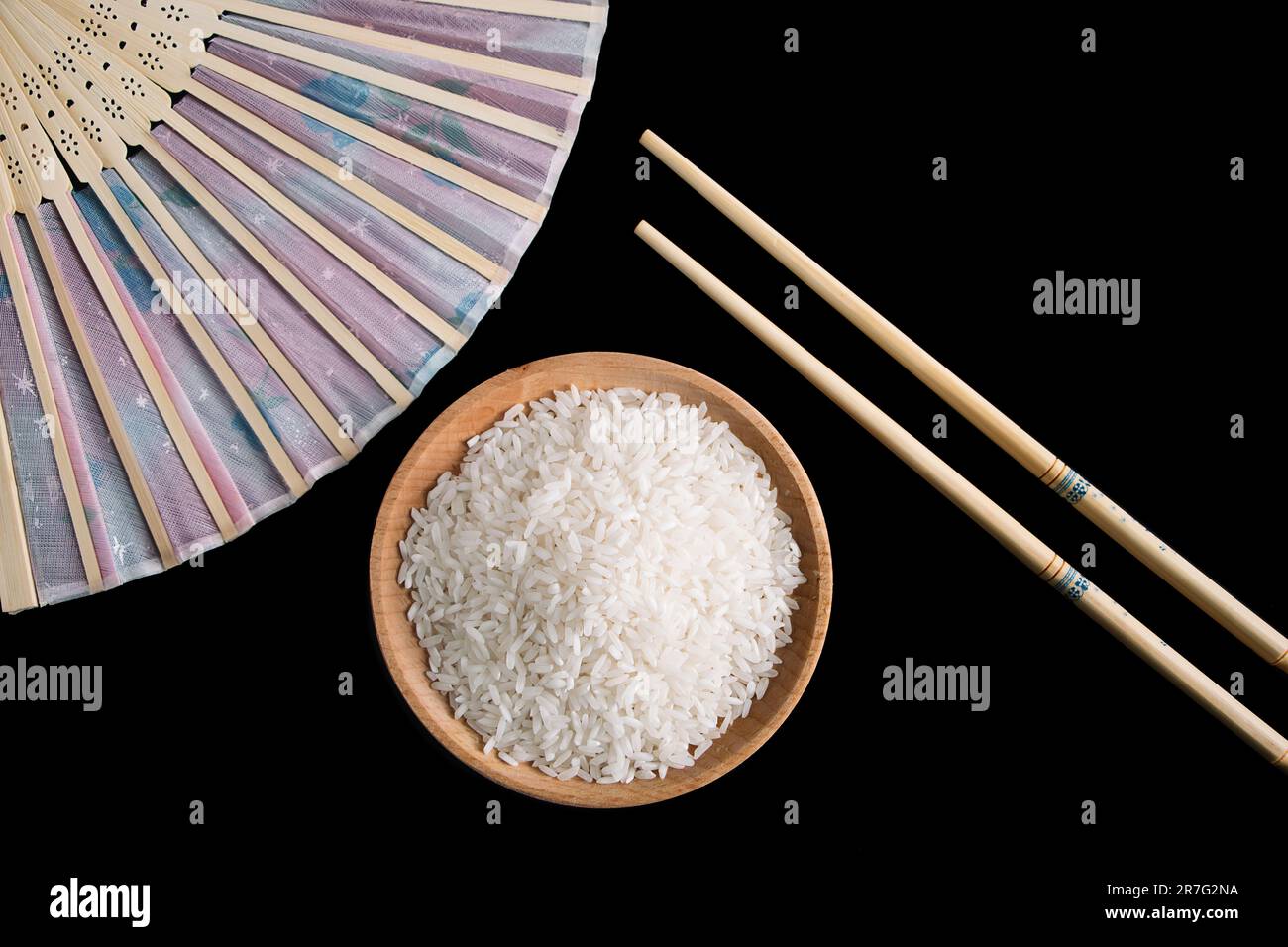 Raw white rice, hand fan and chopsticks on black background. Long ...