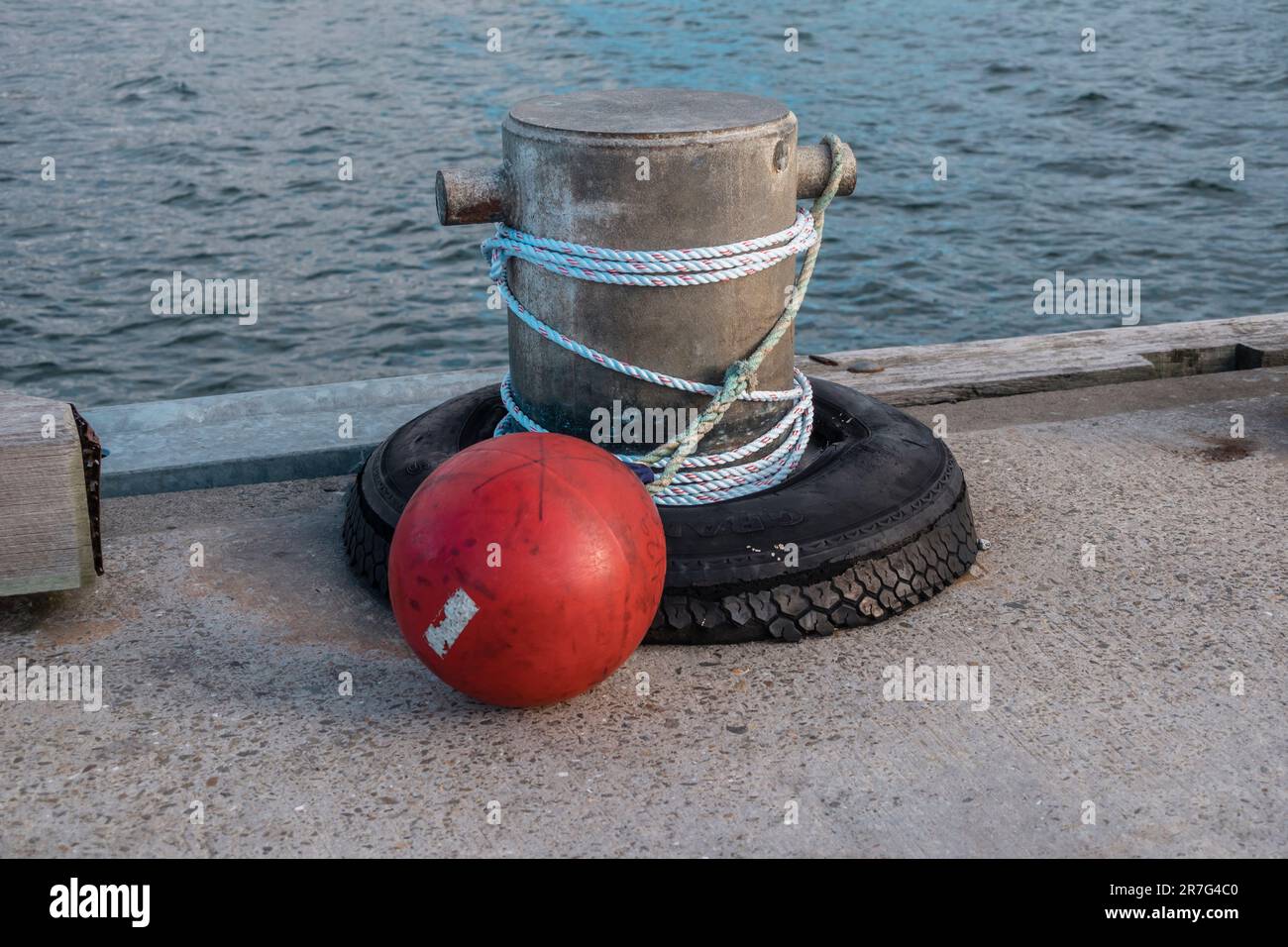 Photograph of white rope wrapped around a steel boat bollard with a red ...