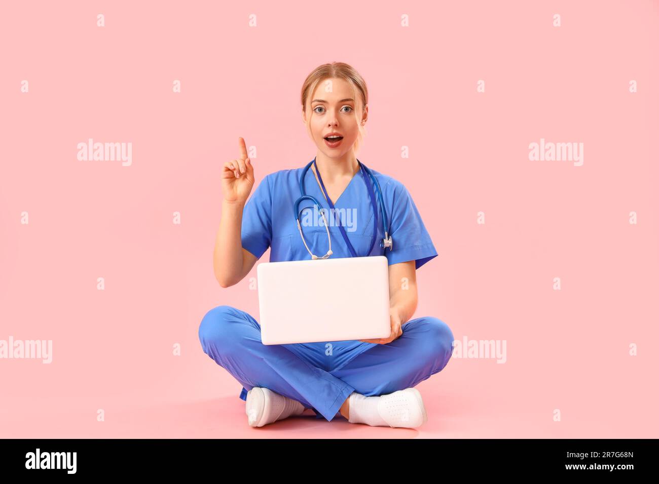 Female medical intern with laptop pointing at something on pink ...