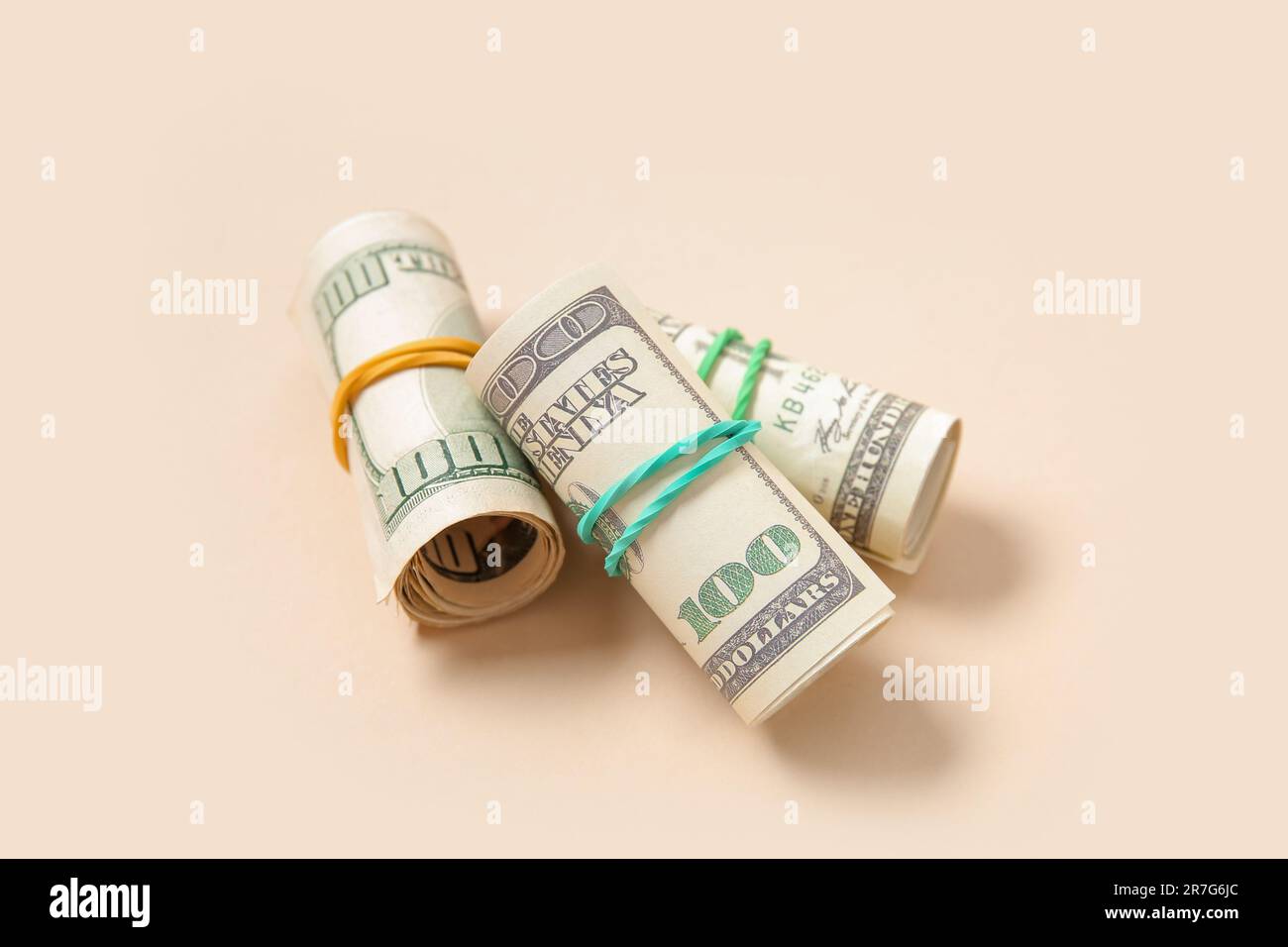 Rolls of one hundred dollar banknotes tied with rubber bands on beige ...