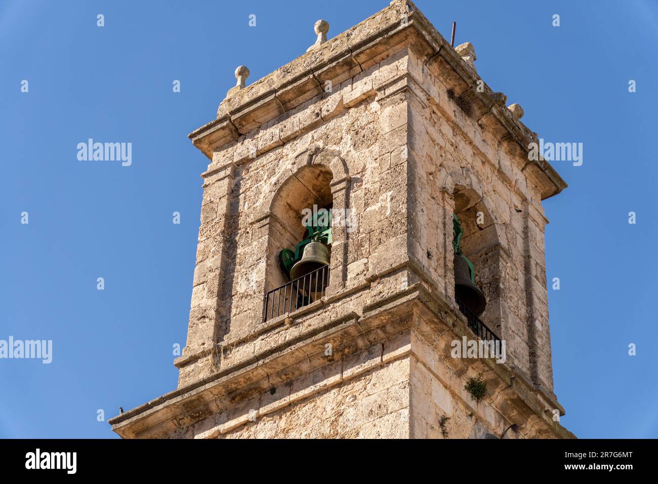 A stone tower stands tall against a clear blue sky, with a bell visible ...