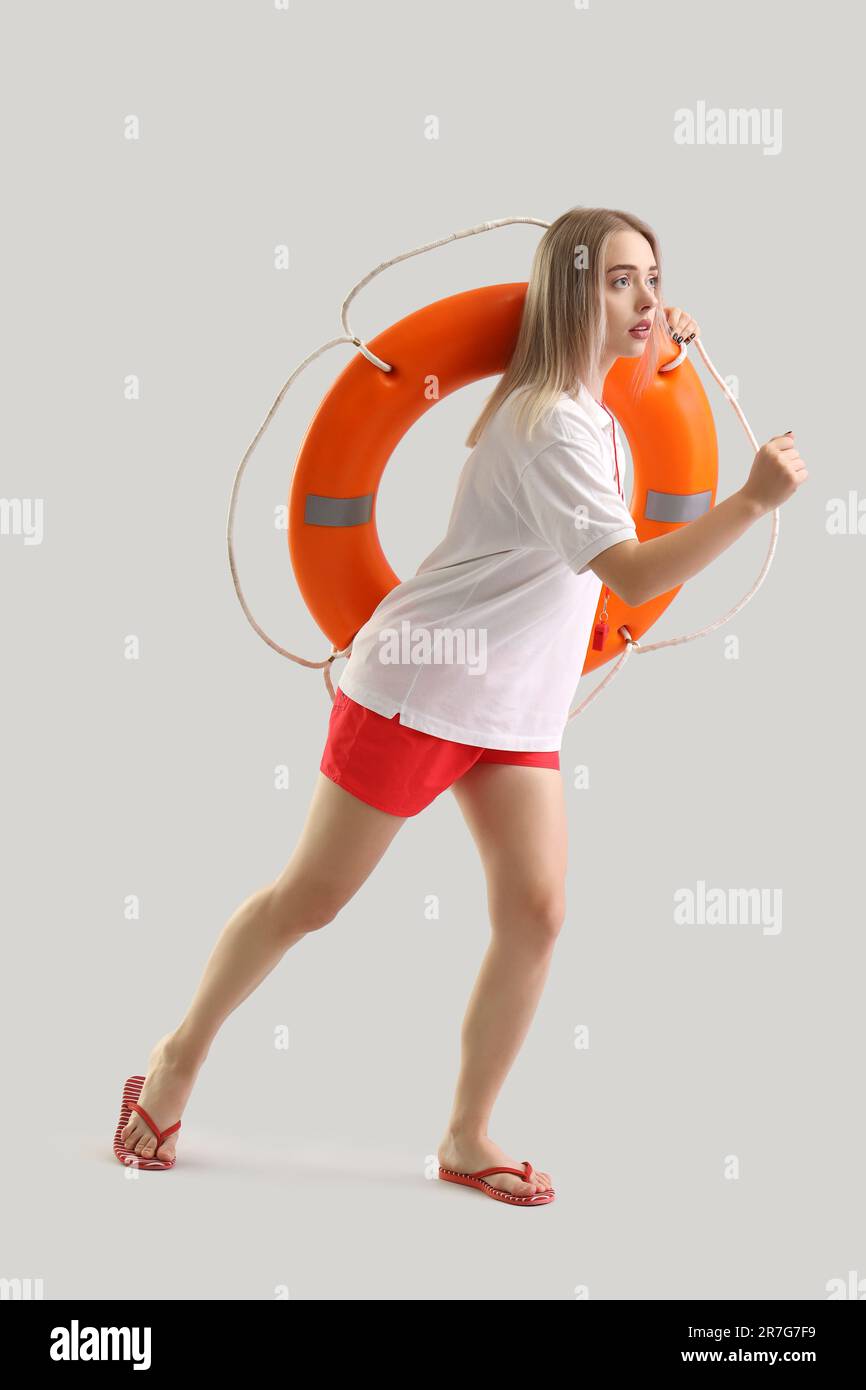 Female lifeguard with ring buoy running on light background Stock Photo ...