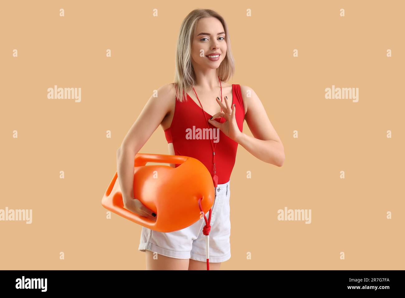 Female lifeguard with rescue buoy showing OK on beige background Stock ...
