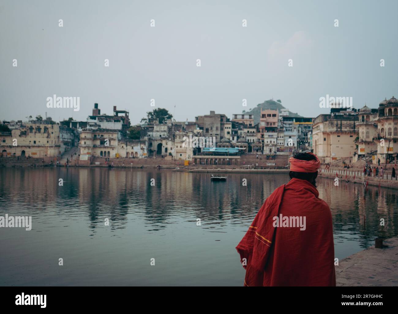 A young adult stands on the shoreline of a body of water, wearing a red ...