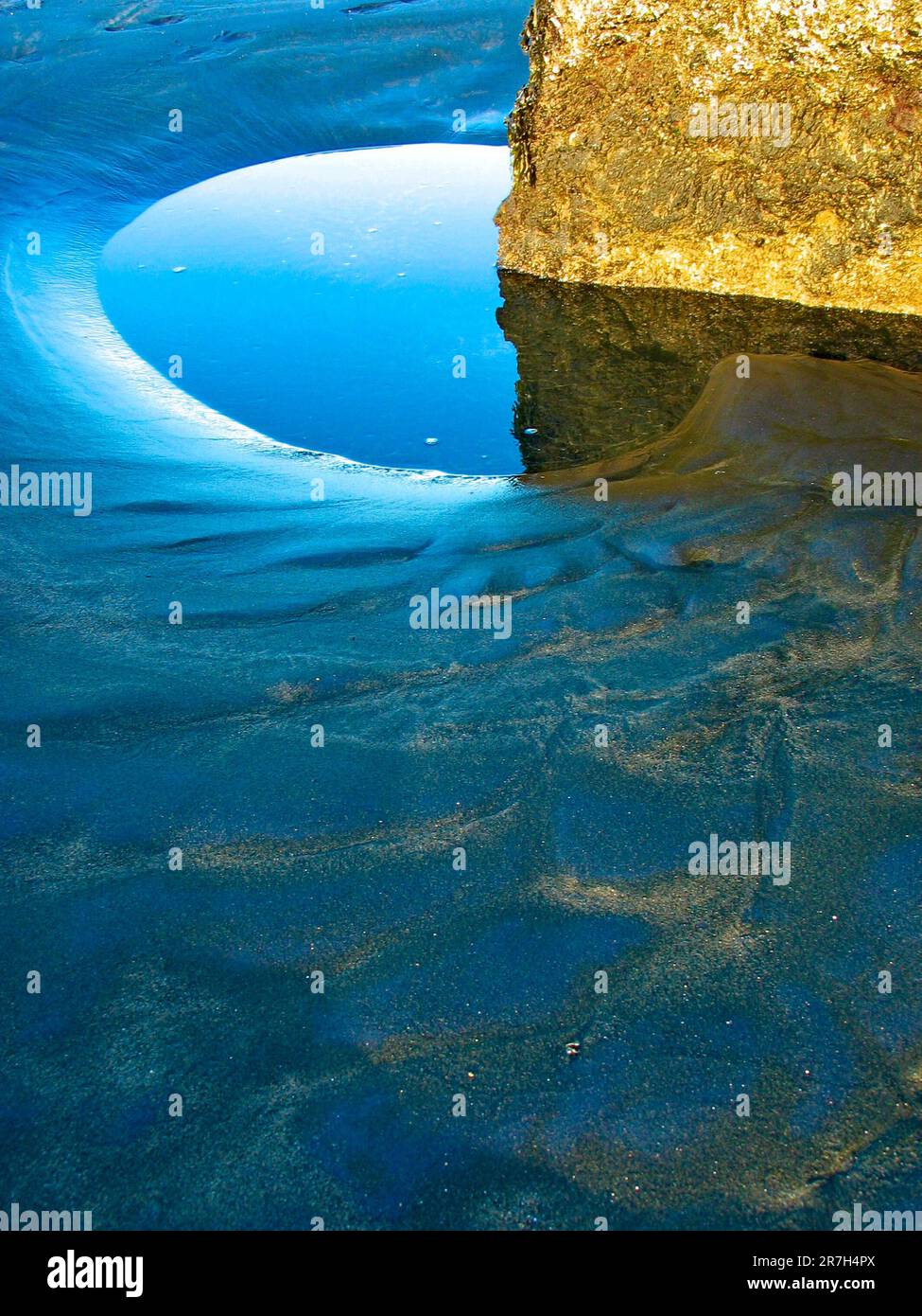 Sky reflected in a small blue puddle, black basalt sand, New Zealand ...