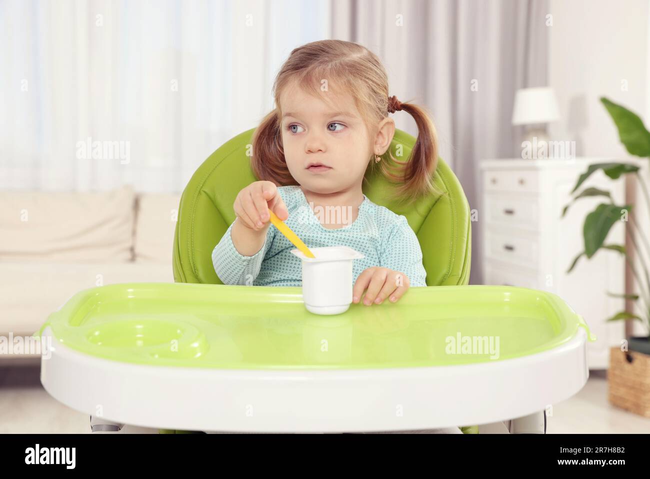 Cute little child eating tasty yogurt from plastic cup with spoon in ...
