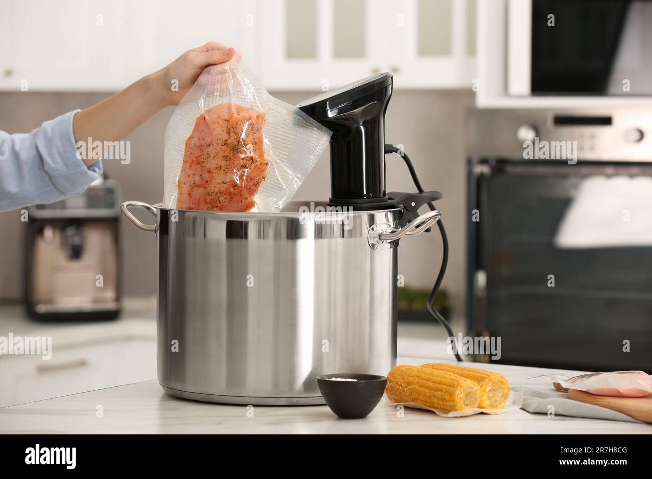 Woman putting vacuum packed meat into pot with sous vide cooker in ...