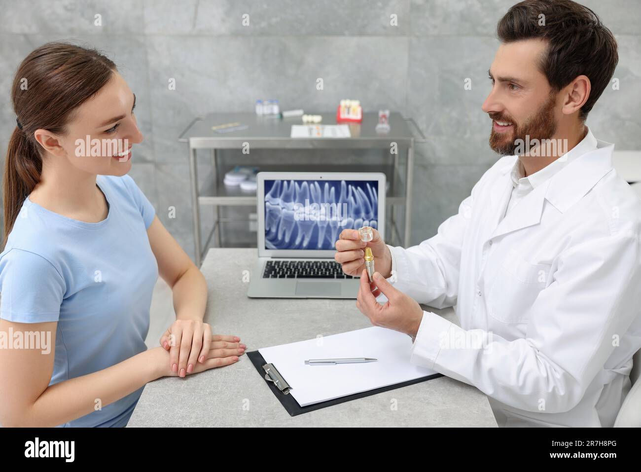 Doctor showing patient educational model of dental implant in clinic ...