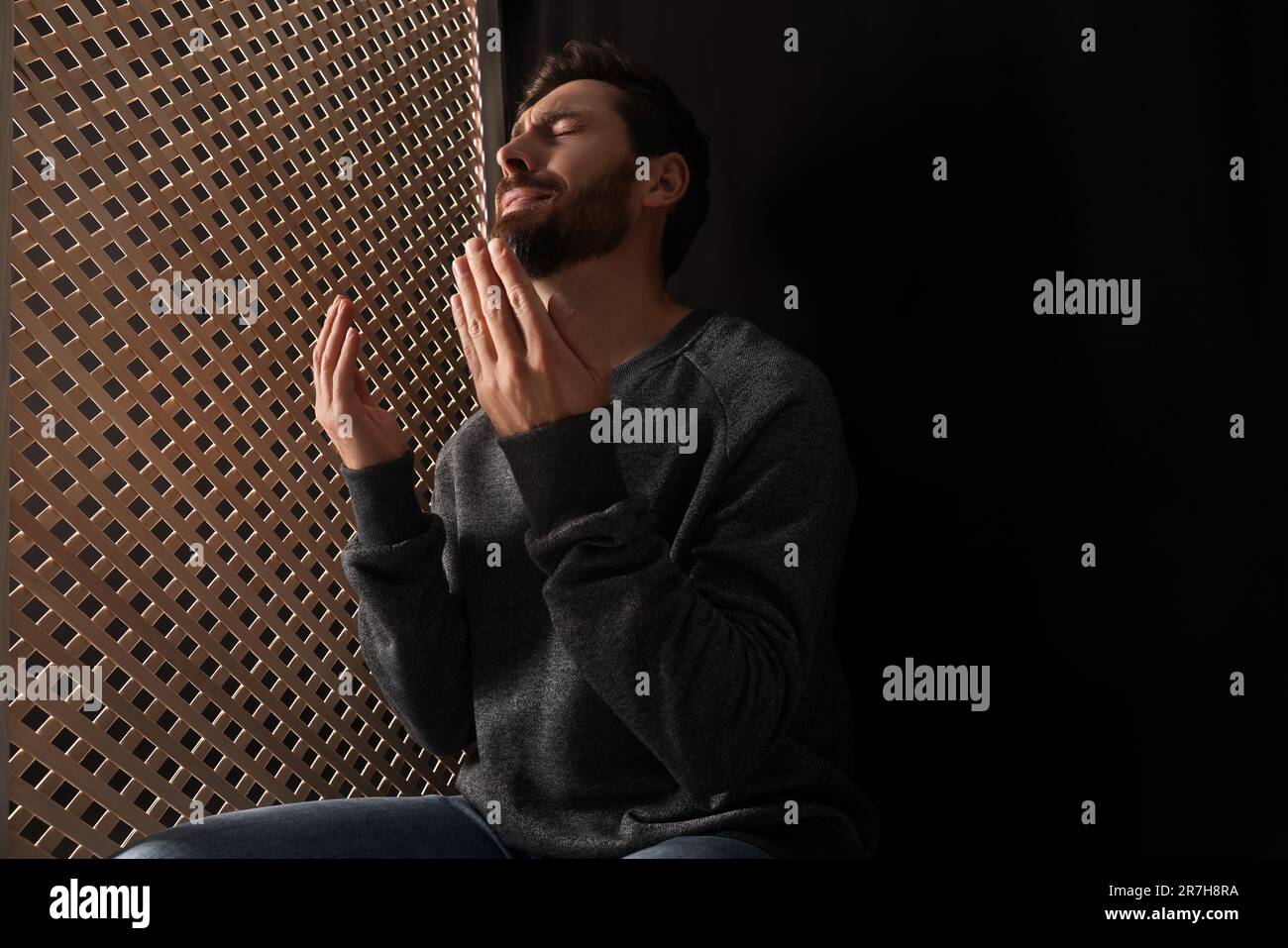 Upset man praying to God during confession in booth, space for text ...