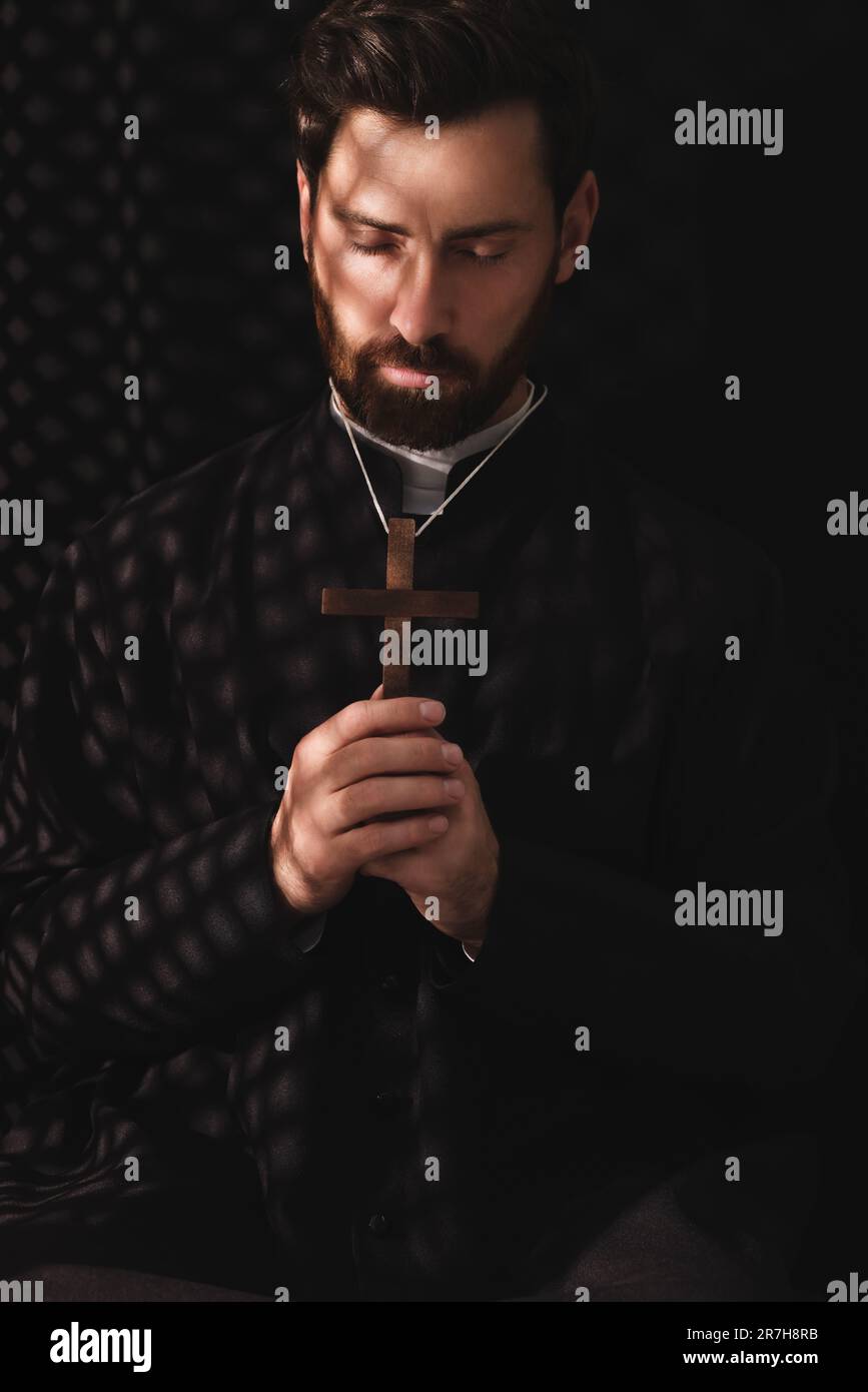Catholic priest in cassock holding cross and praying to God in ...