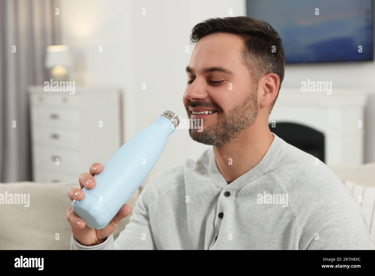 Man drinking from light blue thermo bottle indoors Stock Photo - Alamy