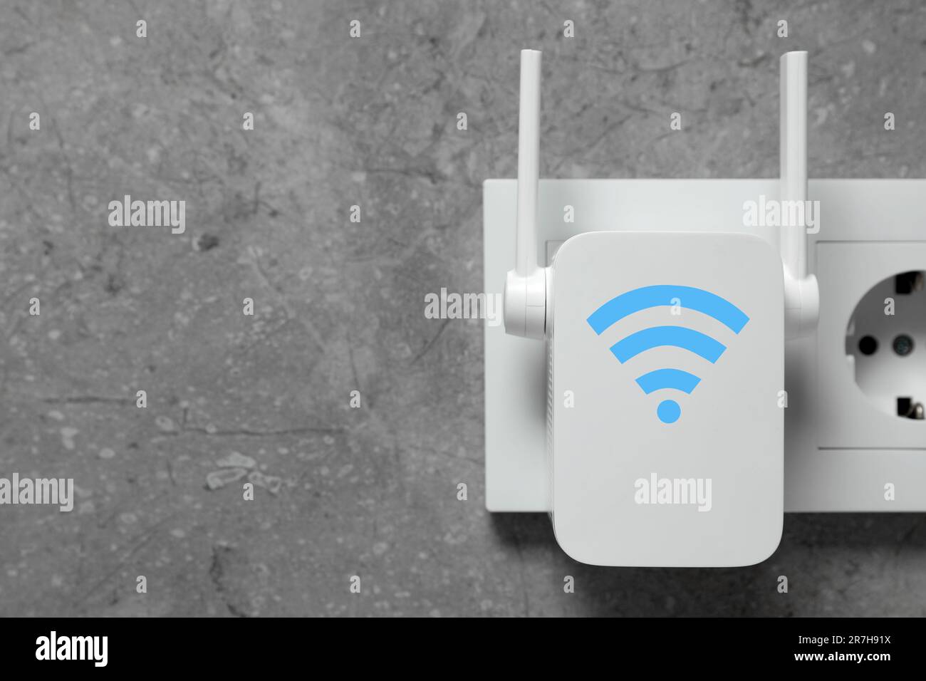 New modern repeater with Wi-Fi symbol plugged into socket on concrete ...