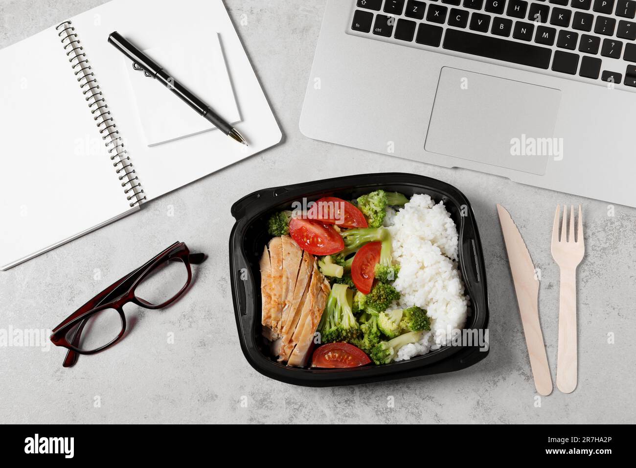 Container with tasty food, laptop, plastic cutlery and notebook on ...