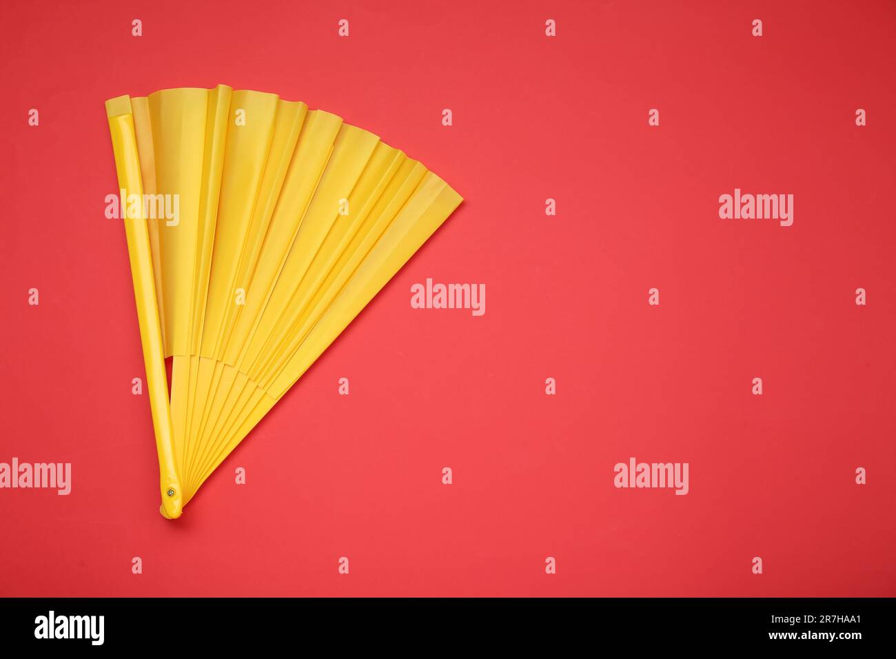 Bright yellow hand fan on red background, top view. Space for text ...