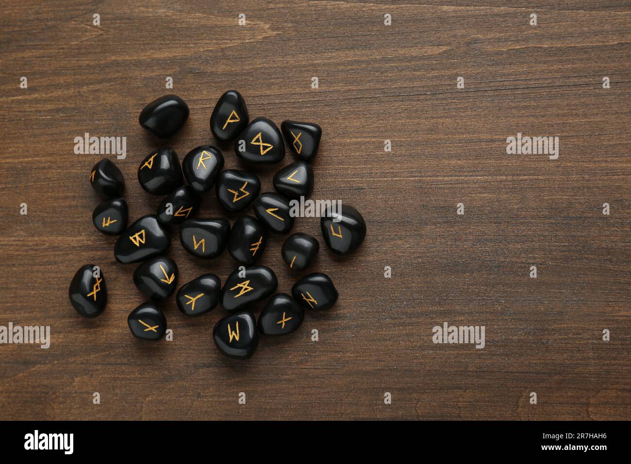 Pile of black rune stones on wooden table, flat lay. Space for text ...