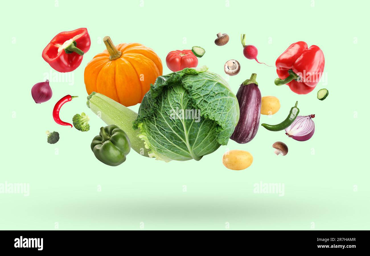 Many different fresh vegetables falling on pale light green background ...