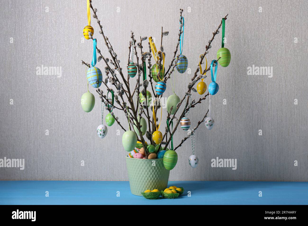 Beautiful willow branches with painted eggs in pot on light blue table ...