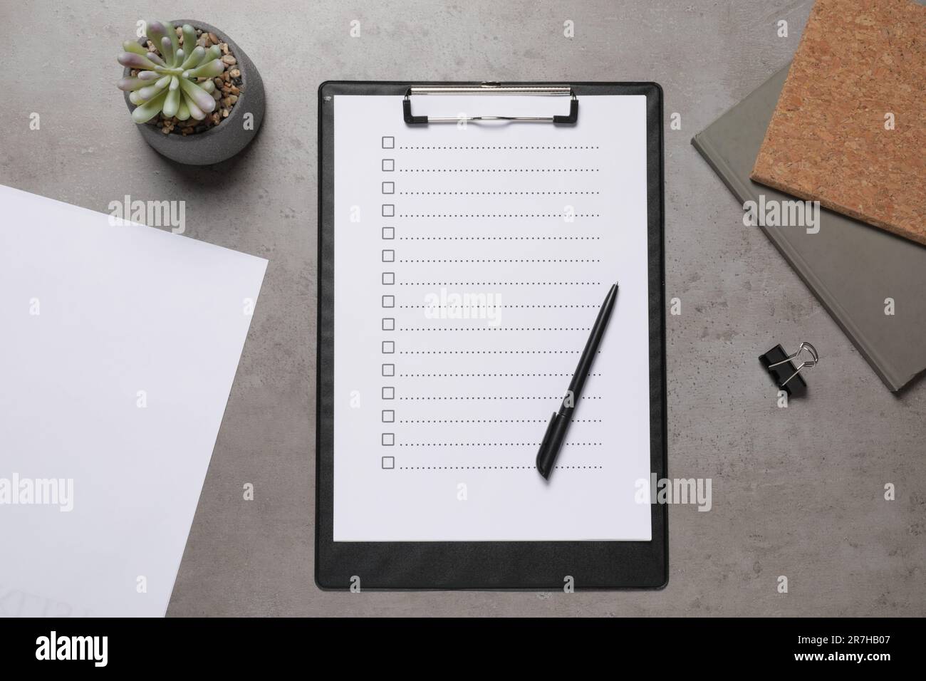 Clipboard with checkboxes, plant and office stationery on grey table ...
