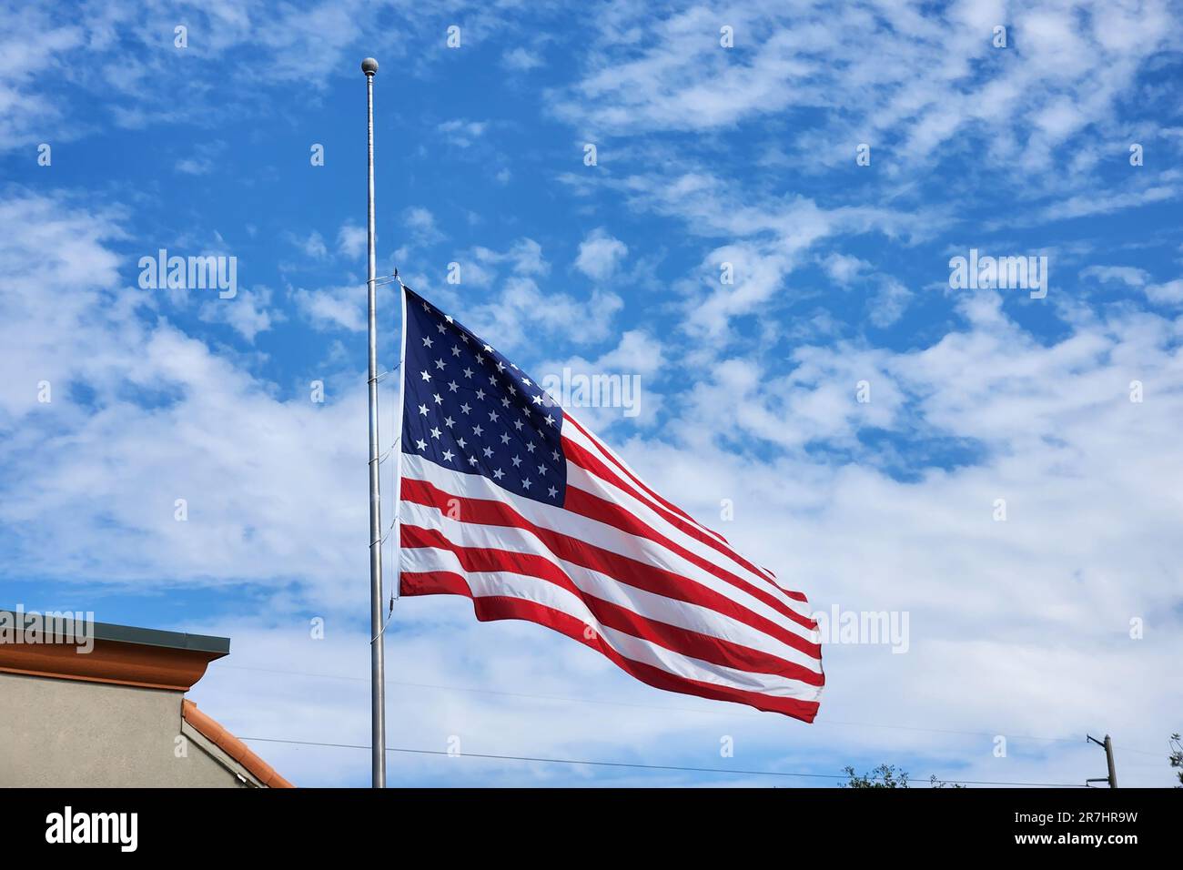 USA national flag waving lowered to half mast on wind against blue sky ...