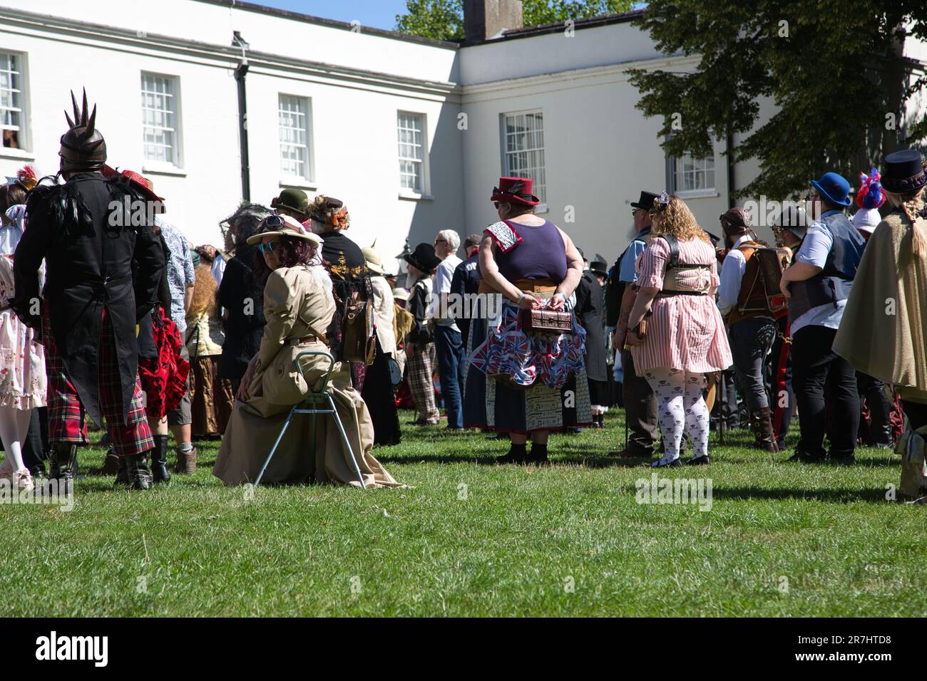 A large congregation of people gathered in the lush grass of a village ...