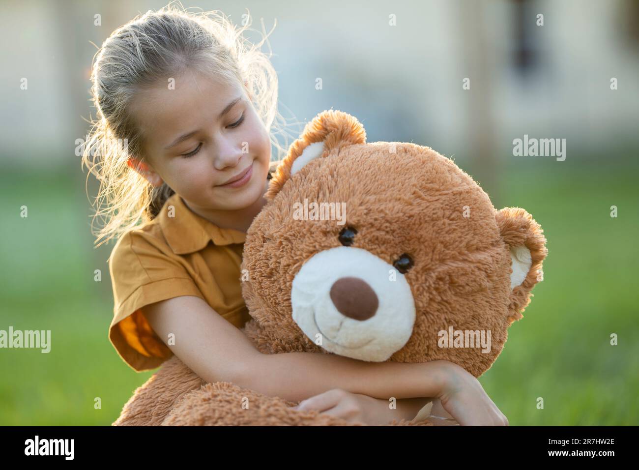 Pretty child girl tenderly embracing her teddy bear friend outdoors on ...