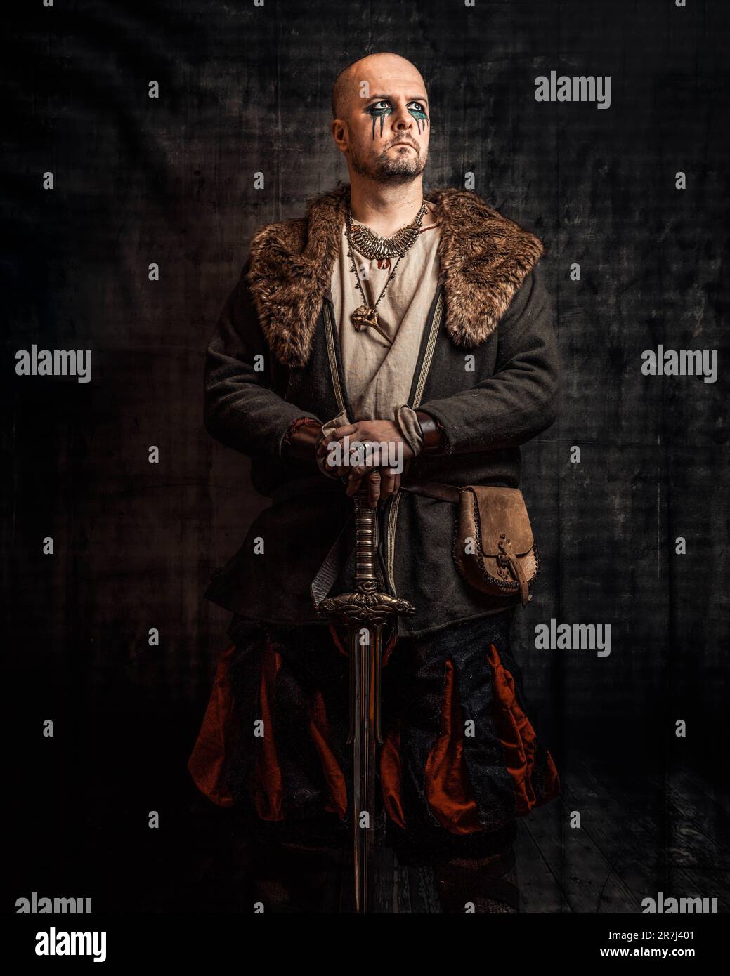 A man dressed in authentic medieval armor sitting against dark ...