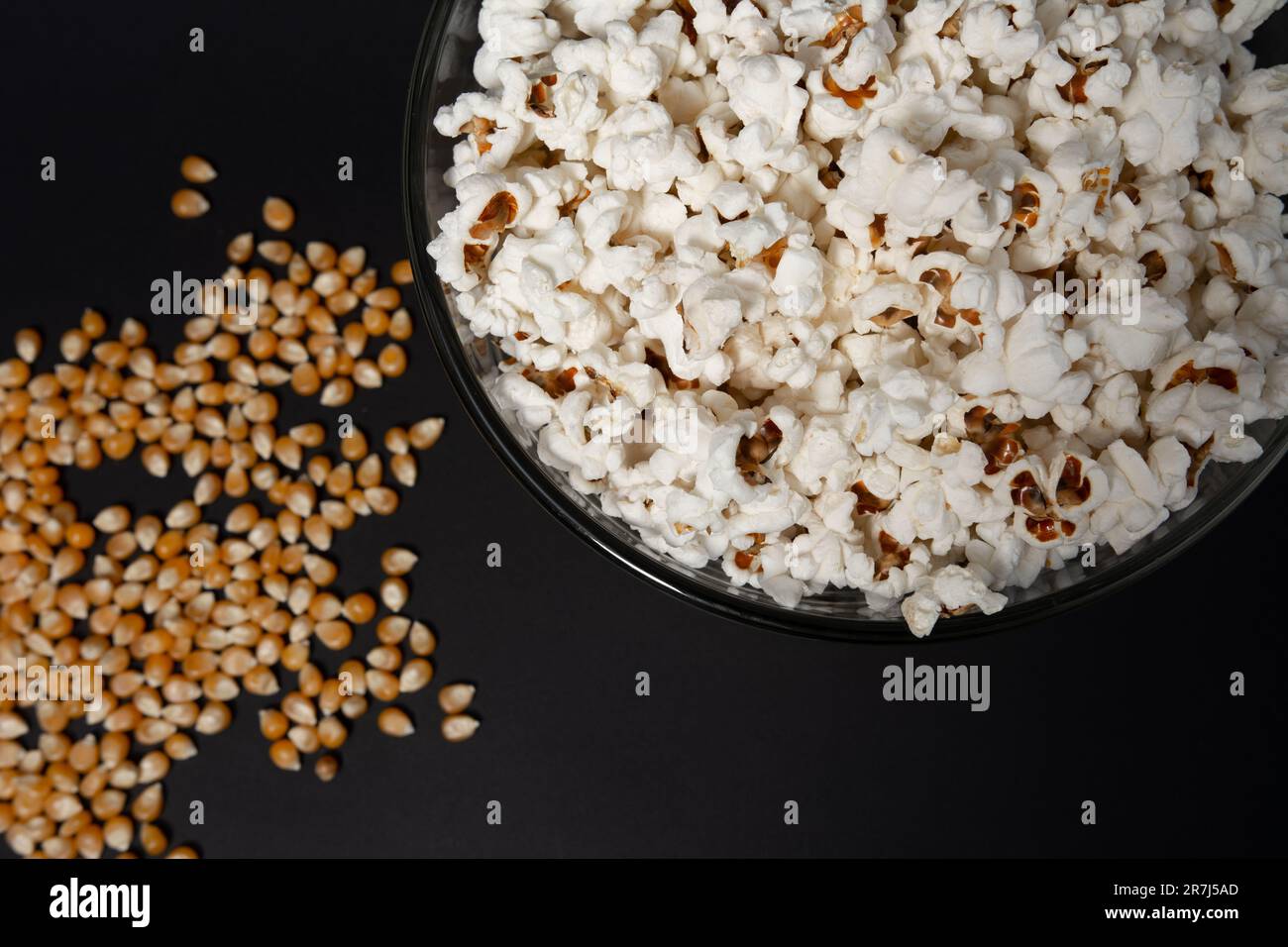 Ready-to-eat popcorn in a glass bowl and corn kernels on a black ...