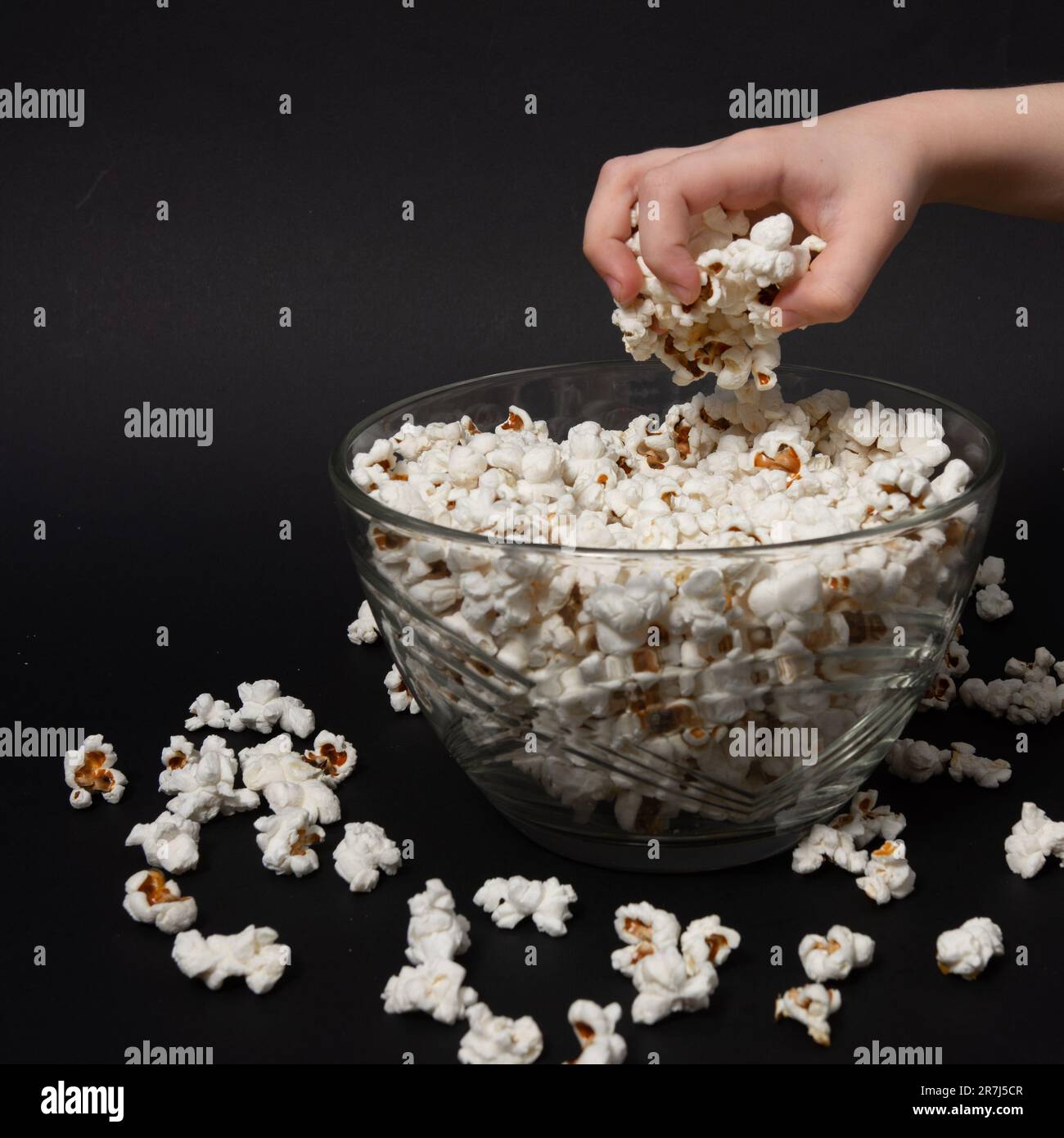a child's hand on a black background takes popcorn from a bowl, freshly ...