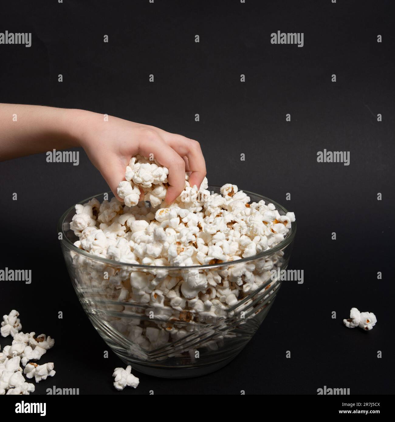 A child's hand reaches for popcorn, which is in a glass bowl, copy ...