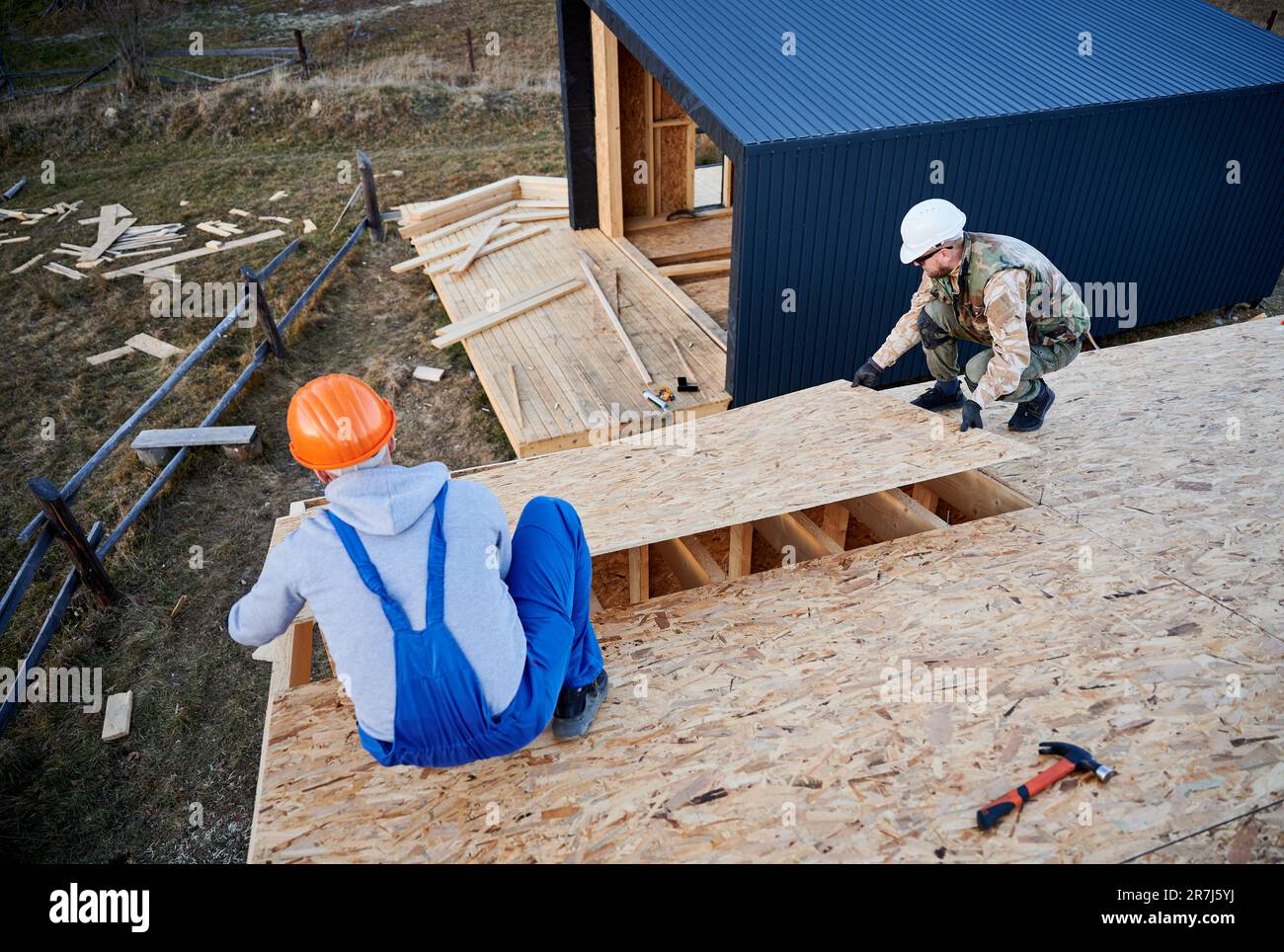 Carpenters mounting wooden OSB board on rooftop of future cottage. Men ...