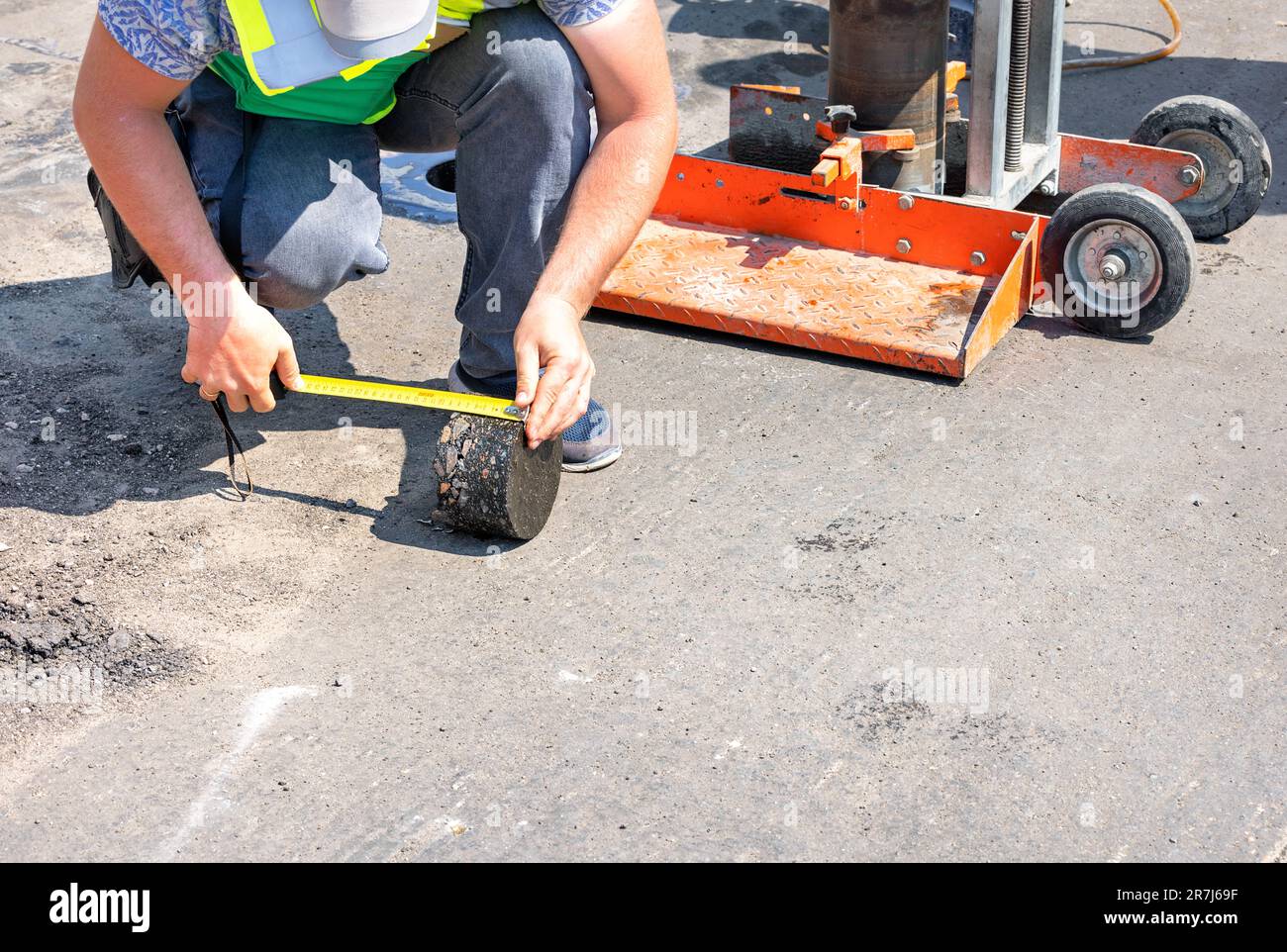 A road service engineer measures a core from an asphalt pavement with a ...