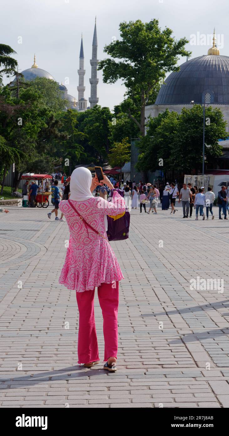 Muslim lady in pink and red clothes with white head scarf takes a photo ...