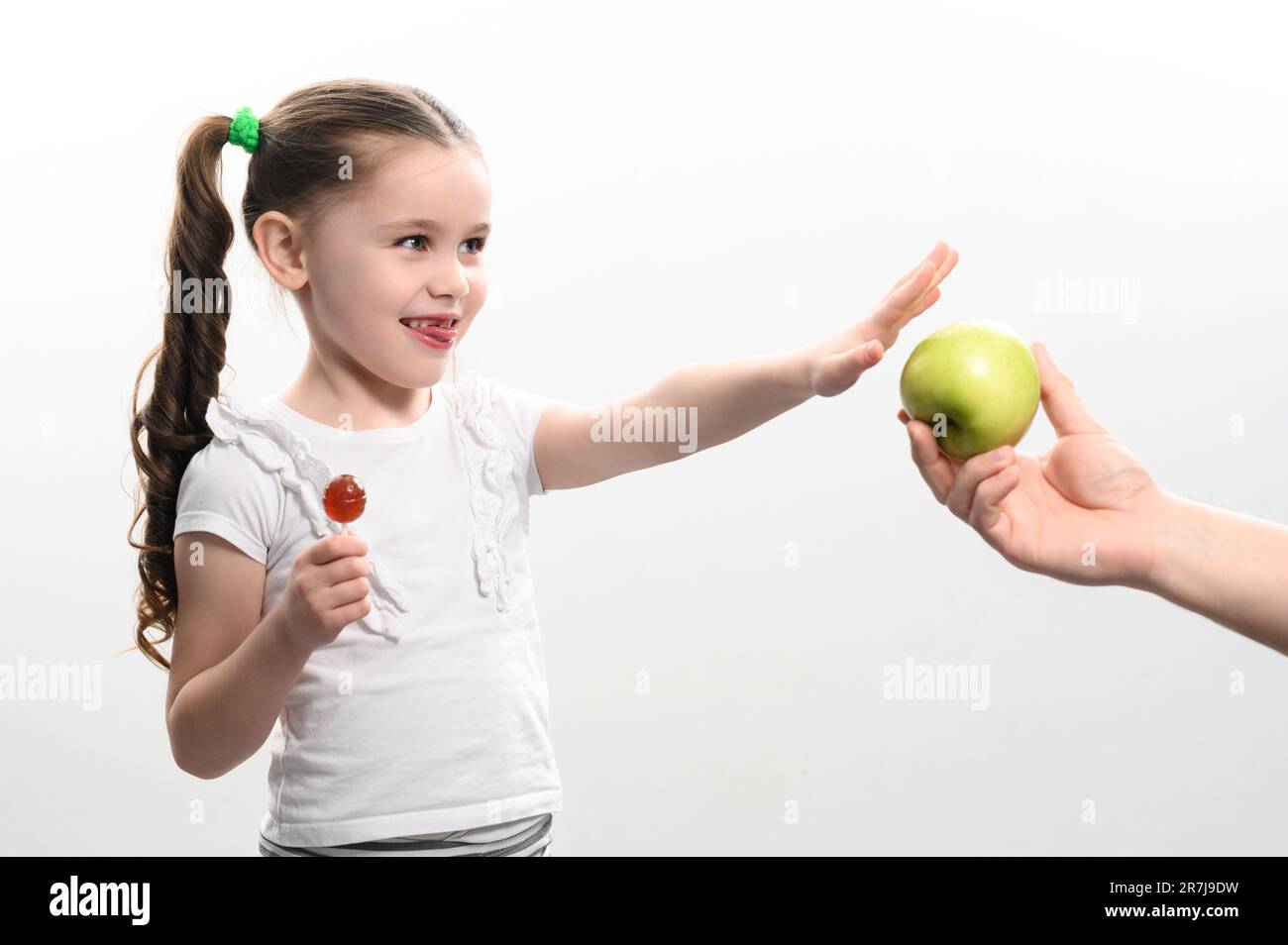 Little girl chooses a lollipop over an apple, sweets and fruits, choice ...