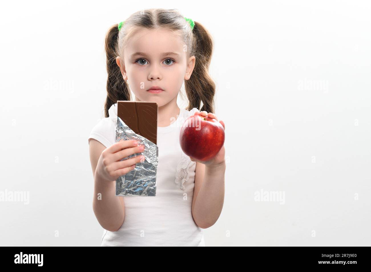 Portrait of a little girl on a white background, she chooses chocolate ...