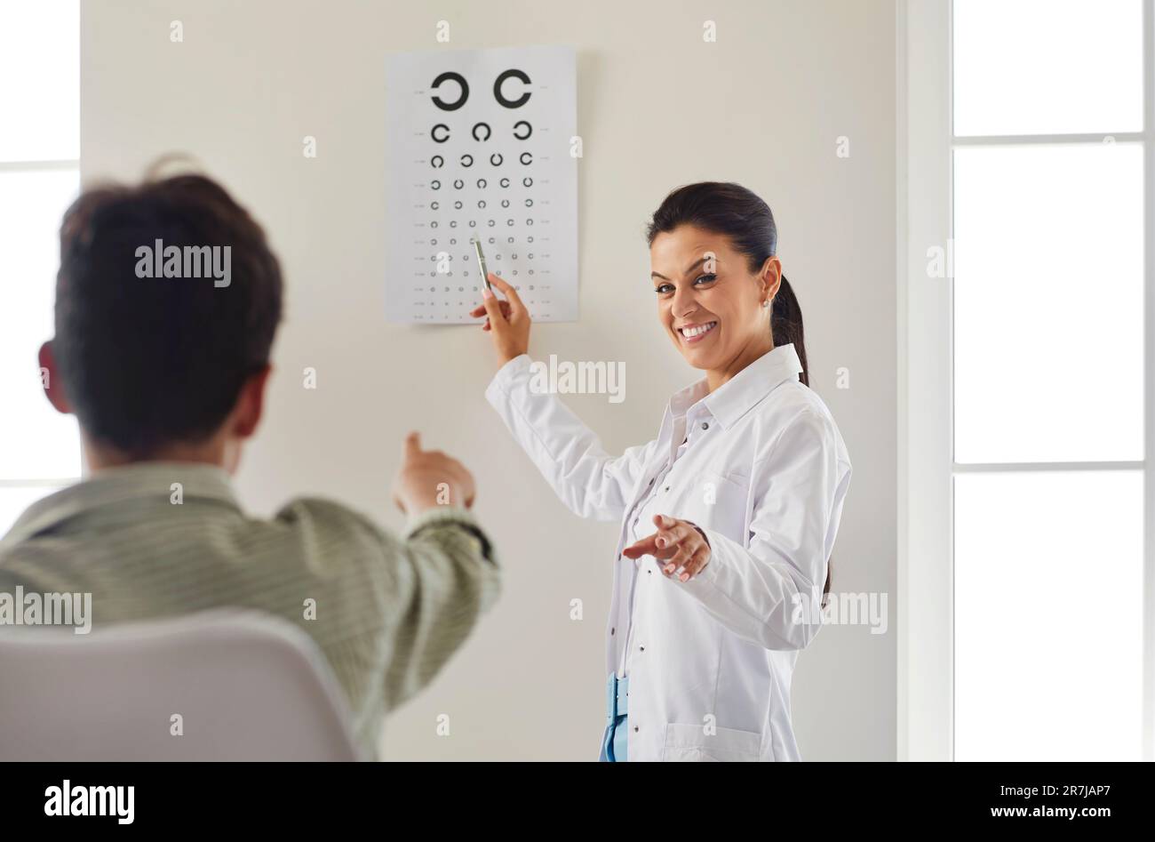 Smiling cheerful female ophthalmologist checking vision of little boy ...