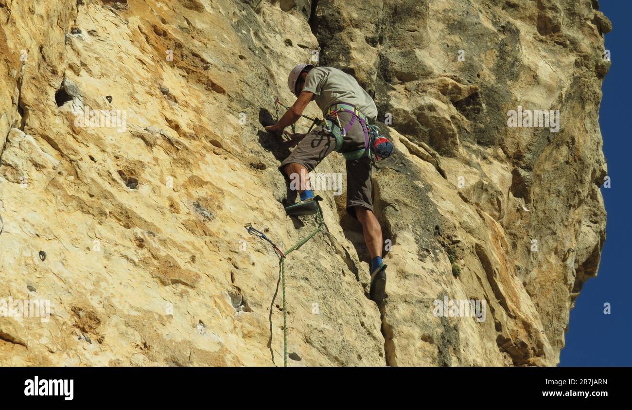 A climber scaling a rocky cliff in a dry and arid desert landscape ...
