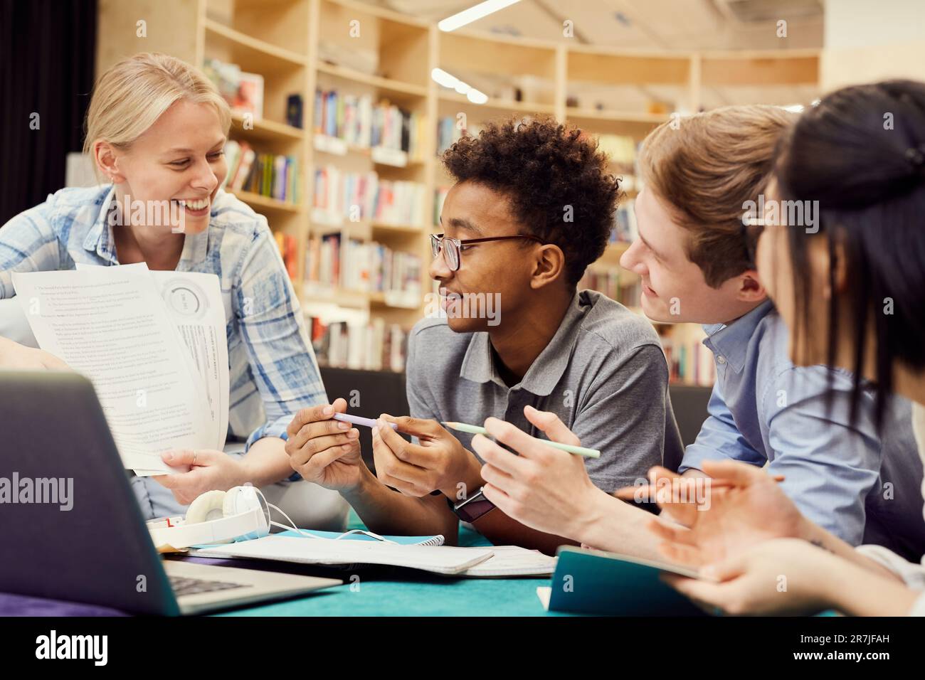 Group of cheerful young multi-ethnic university students sitting in campus lobby and exchanging ...