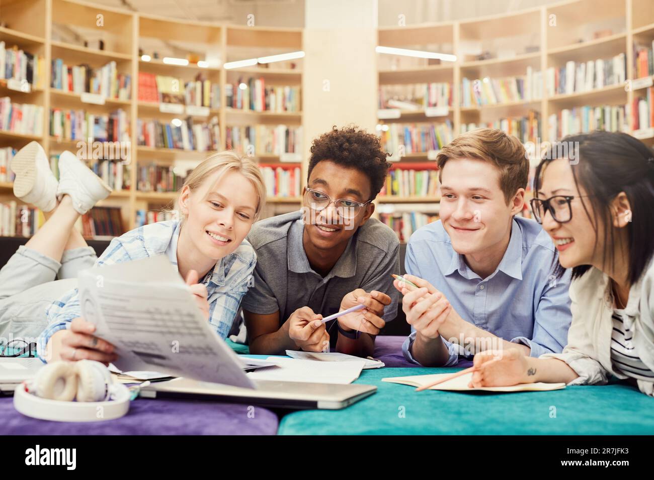 Group of jolly interracial students lying on floor in library and ...