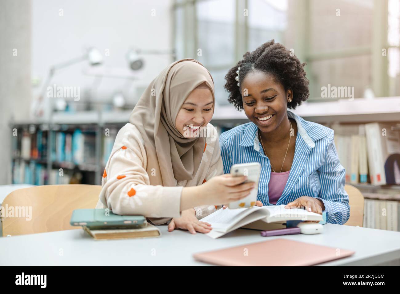 Female students using smartphone while sitting in a library Stock Photo ...