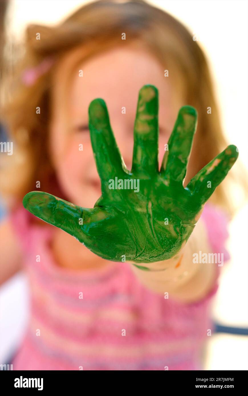 A little blonde girl holds her green painted hand up to the camera ...