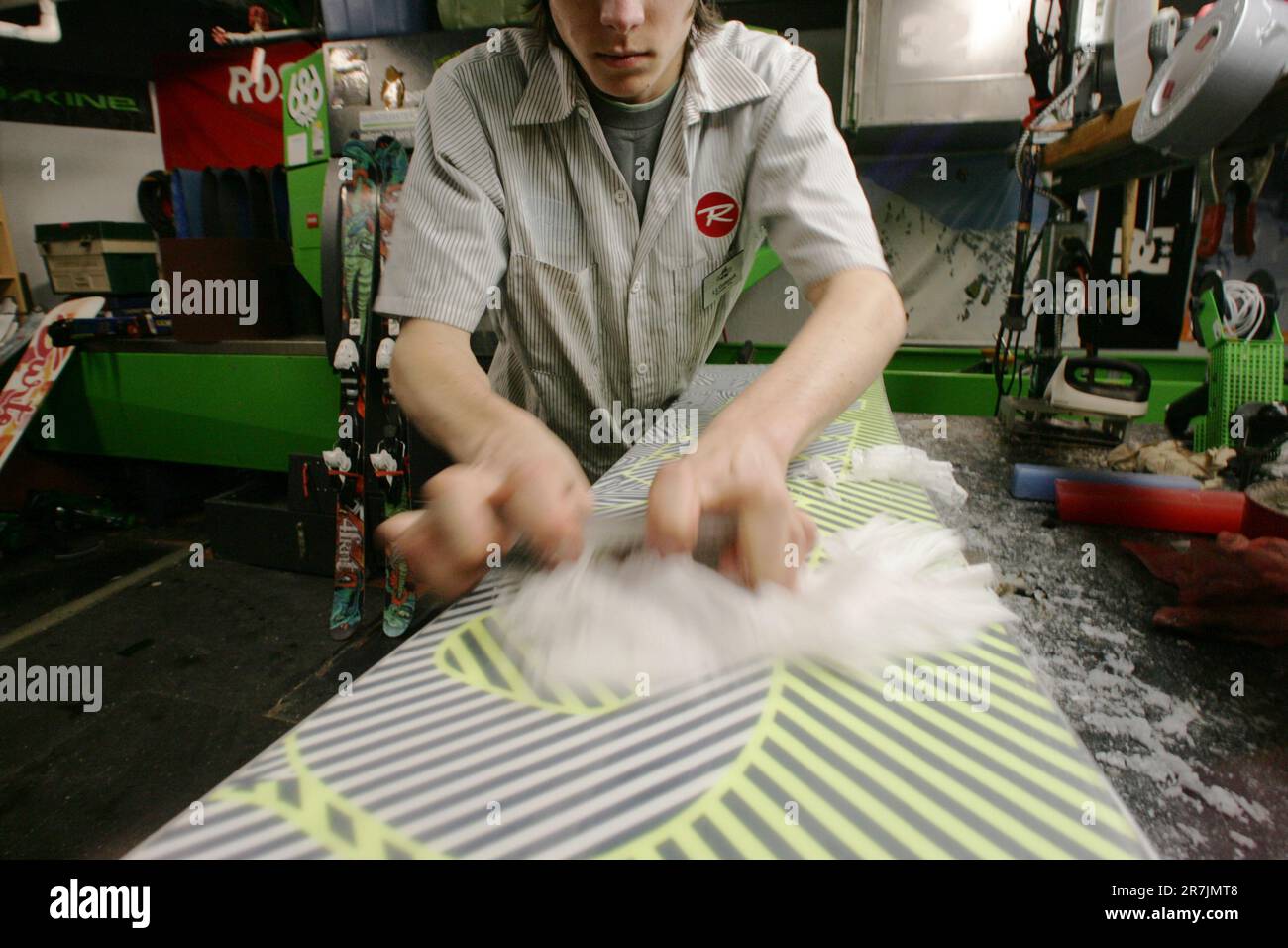 An employee in the ski shop at a mountain resort works on a snowboard ...