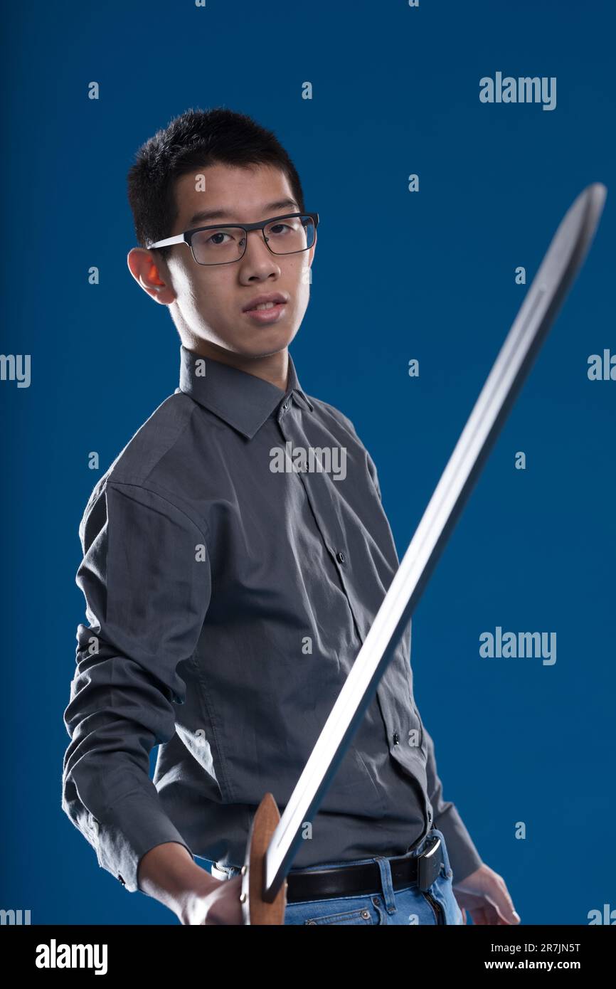 Asian man in workplace attire holds a sword, symbolizing data security and antitheft. He's ...