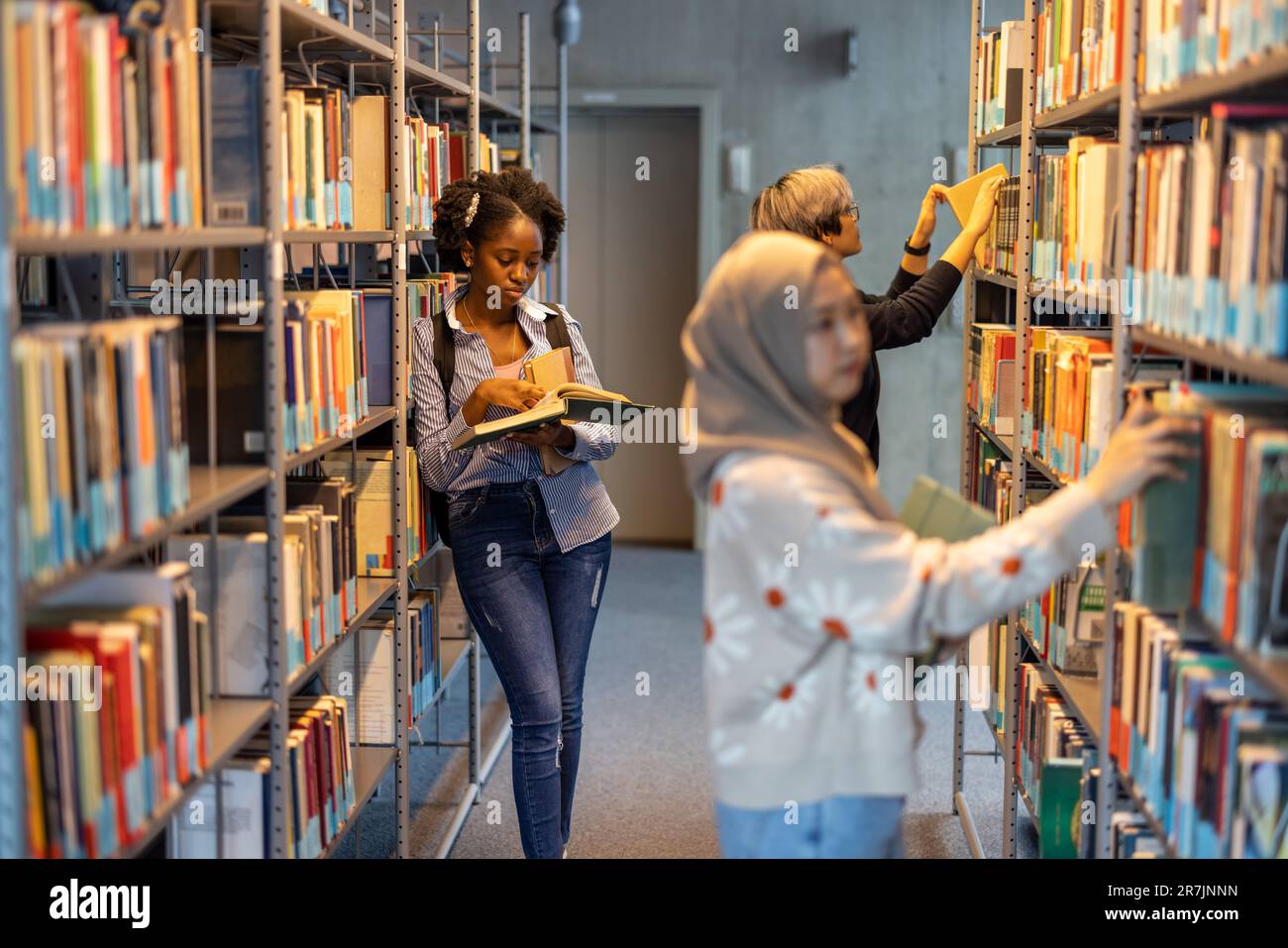 Group of multiethnic students picking books from bookshelf in a library ...