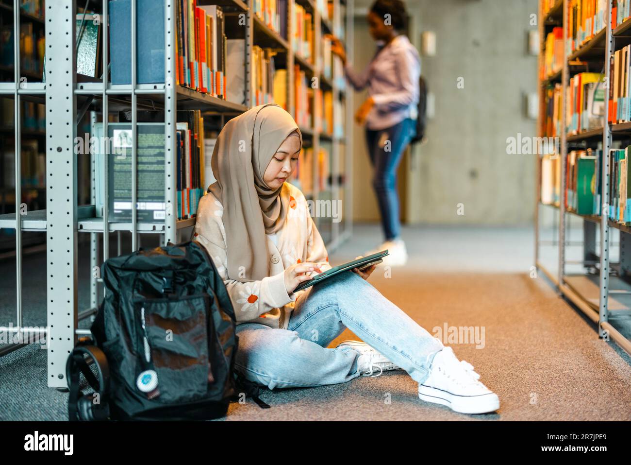 Female muslim student sitting on floor in library and reading book with ...