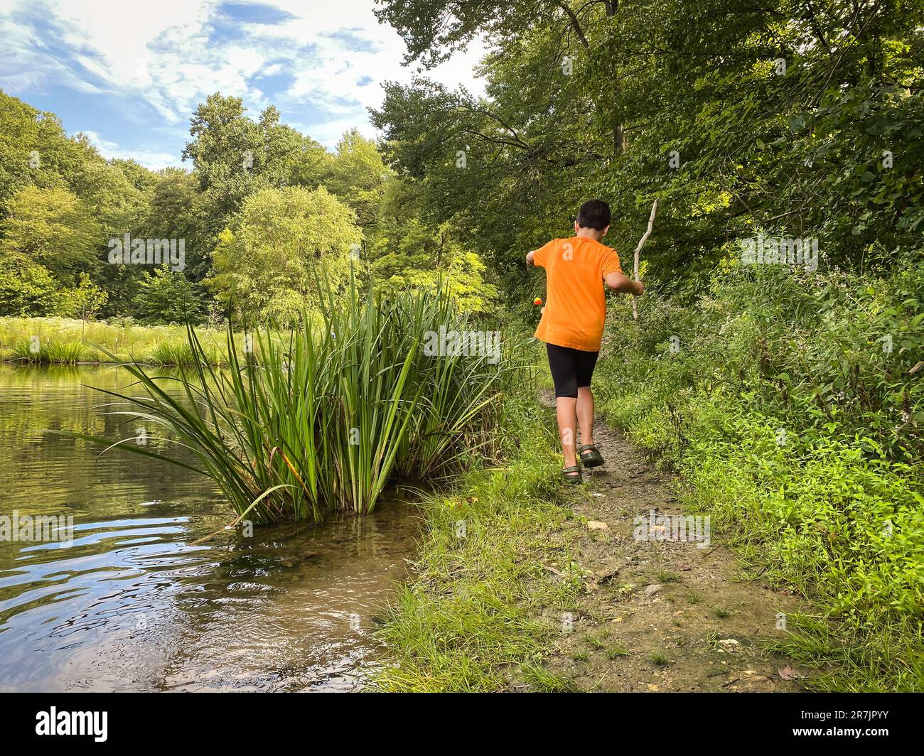 Boy walking down path with fishing rod near lake Stock Photo - Alamy
