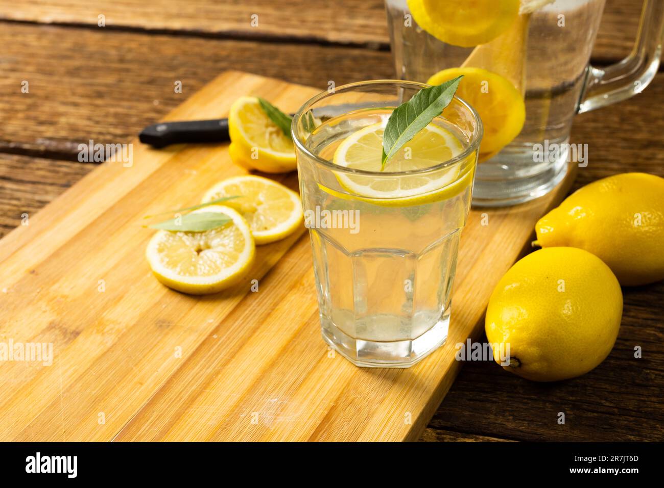 Close-up of lemonade in jug and drinking glass with lemons and leaves ...